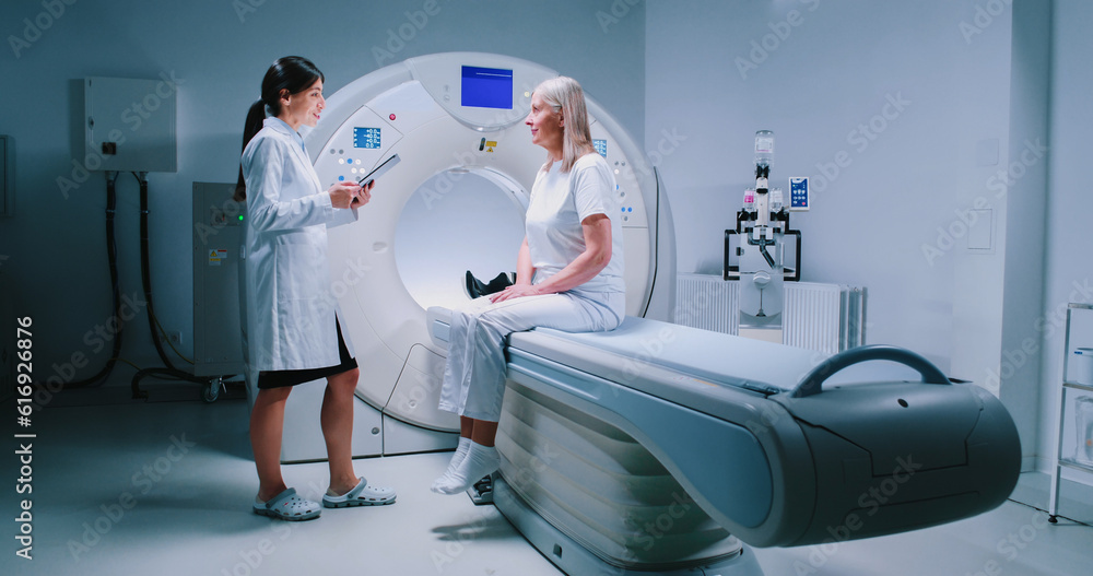 Female doctor gestures and points to MRI capsule. Female patient is ...