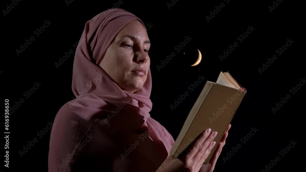 A Muslim woman in a hijab stands on the street and reads the Quran ...
