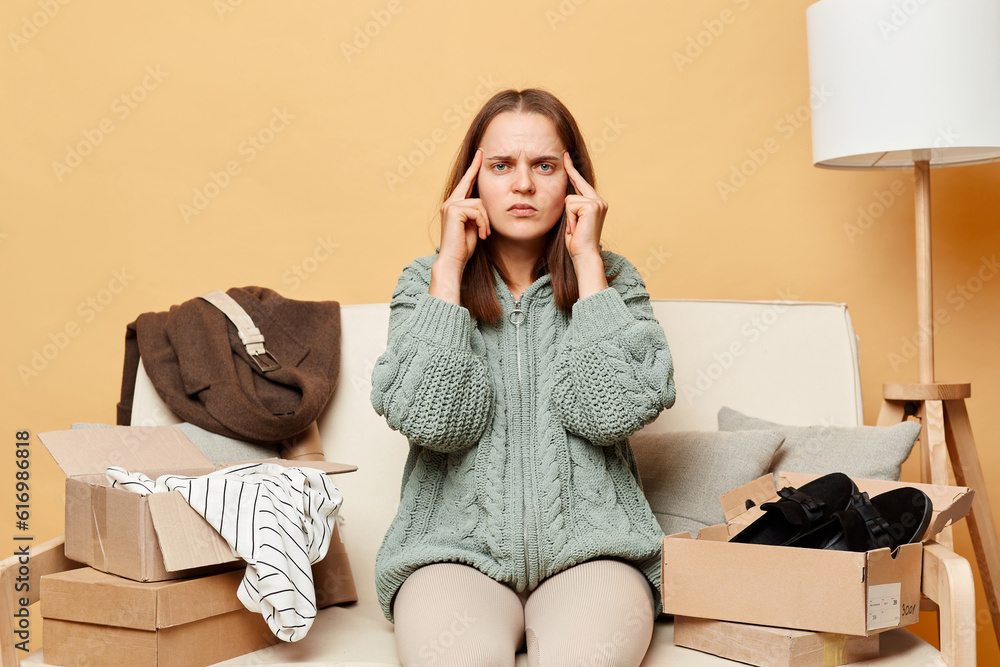 Sad unhealthy sick woman sitting on sofa among boxes with clothing ...