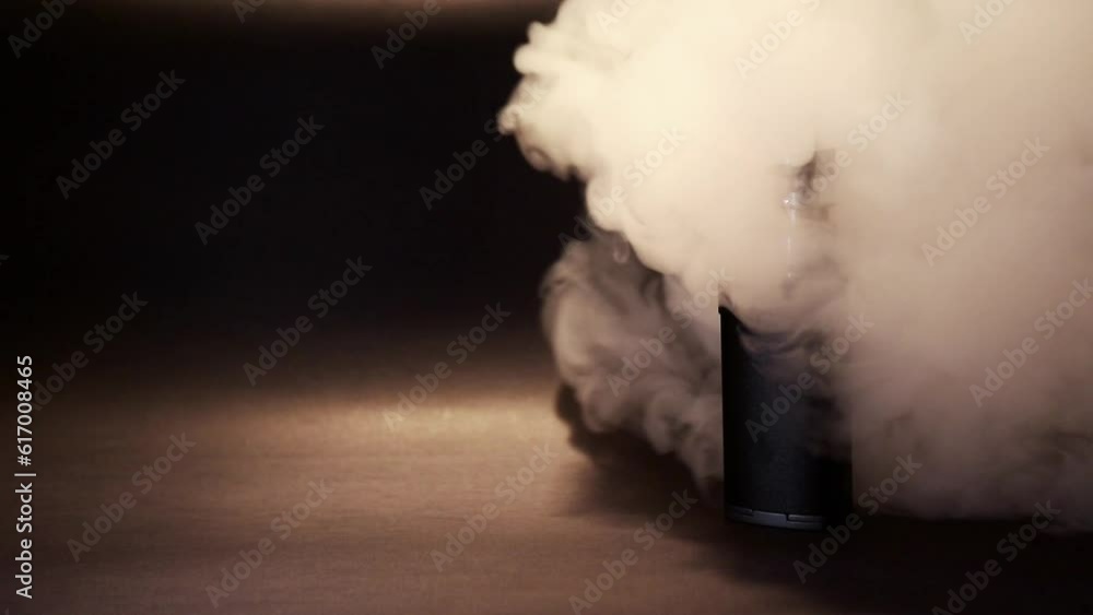 Vape is on a black table in clouds of thick heavy smoke on a black ...