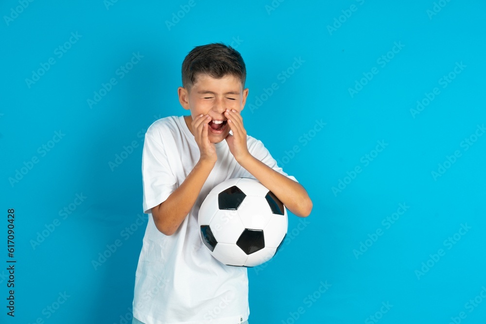 Stupefied Little hispanic boy wearing white T-shirt holding a football ...