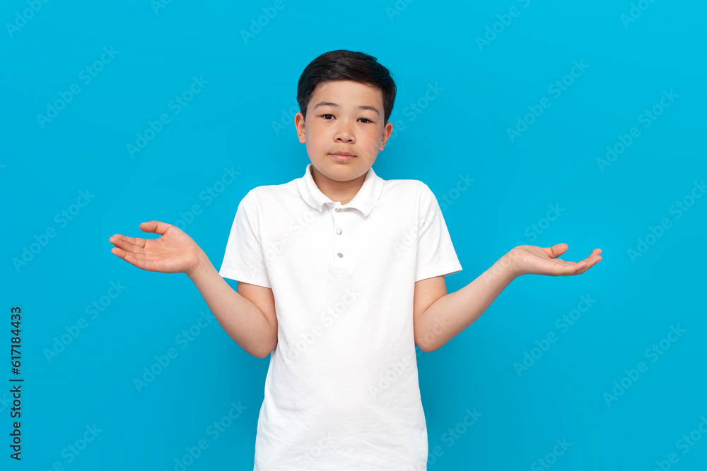 little asian boy in white t-shirt shrugs his shoulders on blue ...