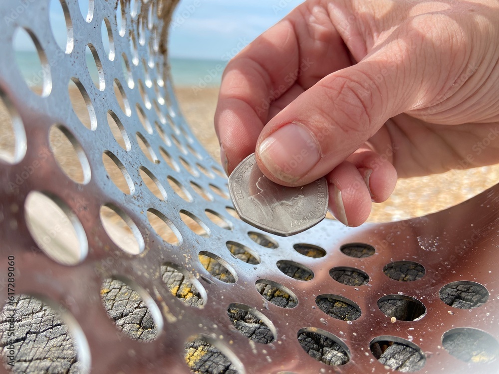 coin in beach sand scoop with metal detector on sand in background on ...