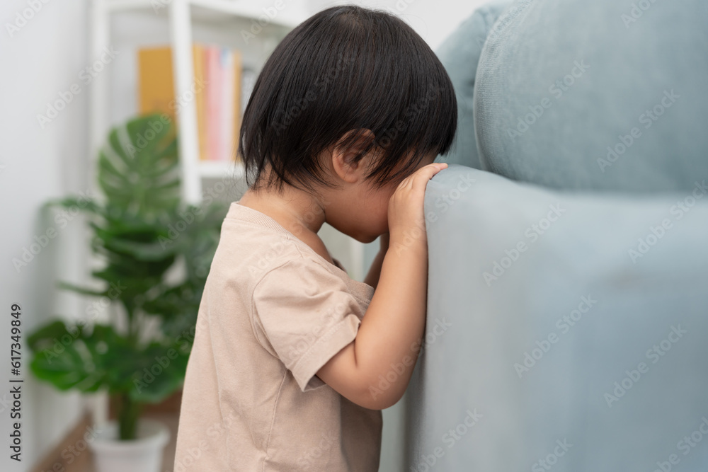 little asian children kid , playing hide and seek standing next a wall ...