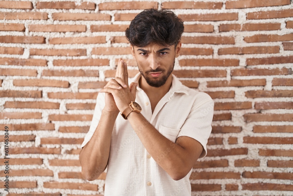Arab man with beard standing over bricks wall background holding ...