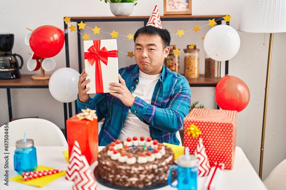 Young chinese man celebrating birthday with cake and present depressed ...