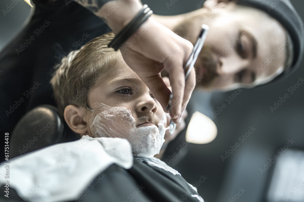 Brutal kid with a shaving foam on the face in the barbershop. He wears ...