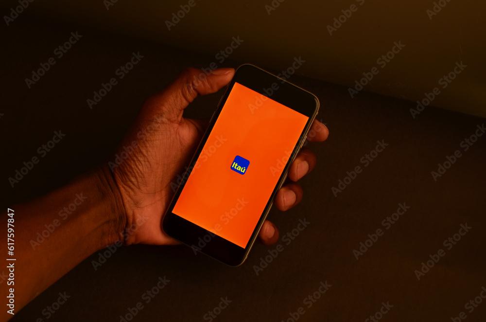 Itau app. Hand holding smartphone with illuminated display in dark ...