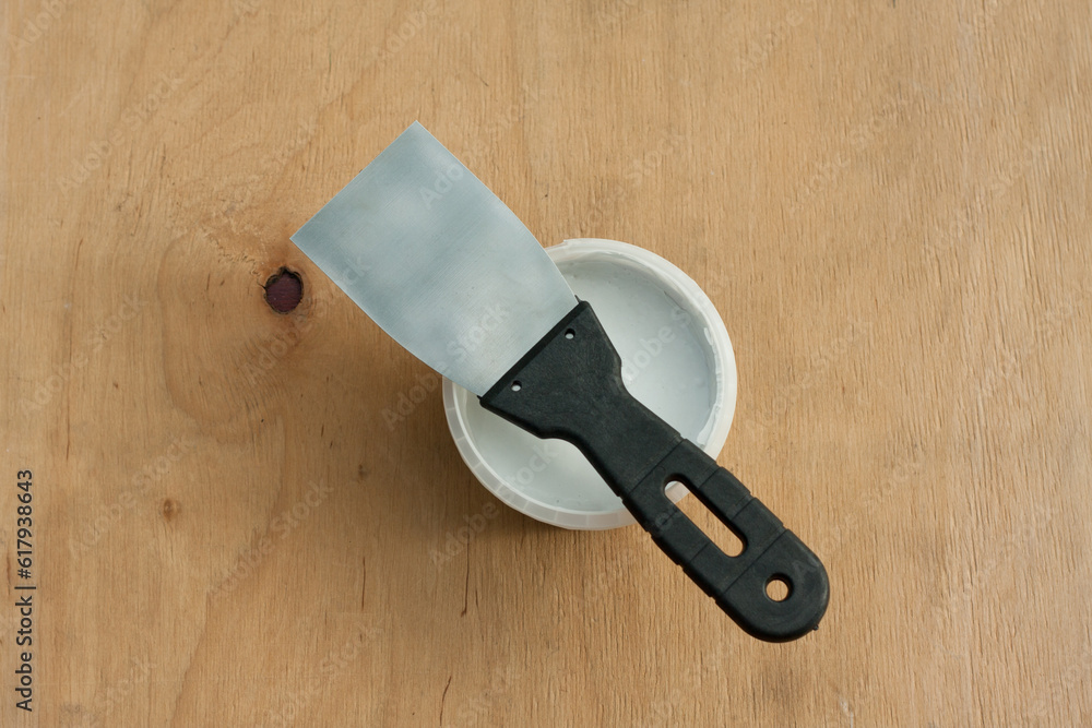 Construction putty knife and can of white putty on plywood surface ...
