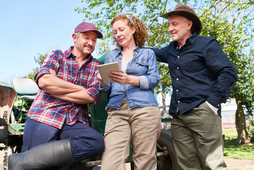 Multicultural farmers discussing over tablet PC by tractor in farm ...
