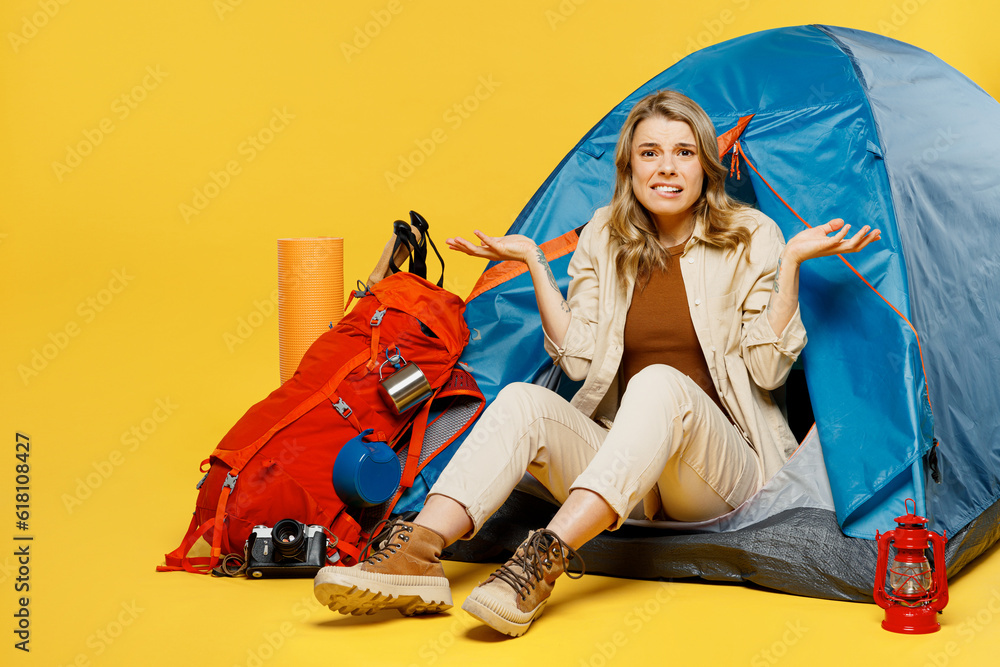 Full body young woman sit near bag with stuff tent spread hands look ...
