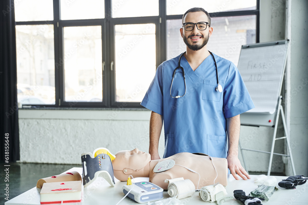 joyful medical instructor looking at camera near CPR manikin ...
