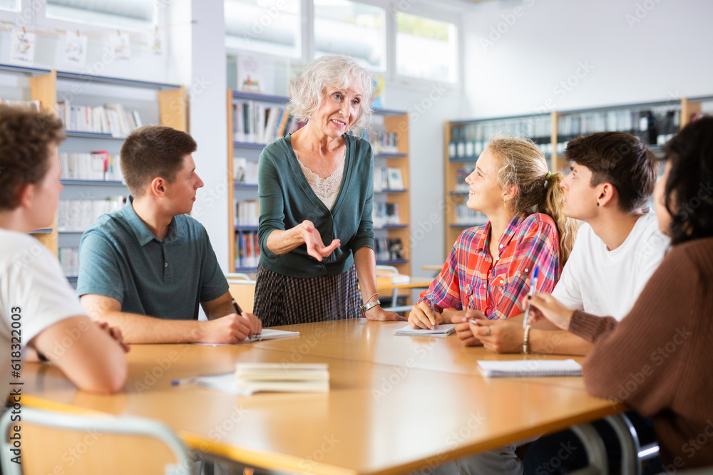 Mature female teacher working with friendly group of schoolgirls and ...