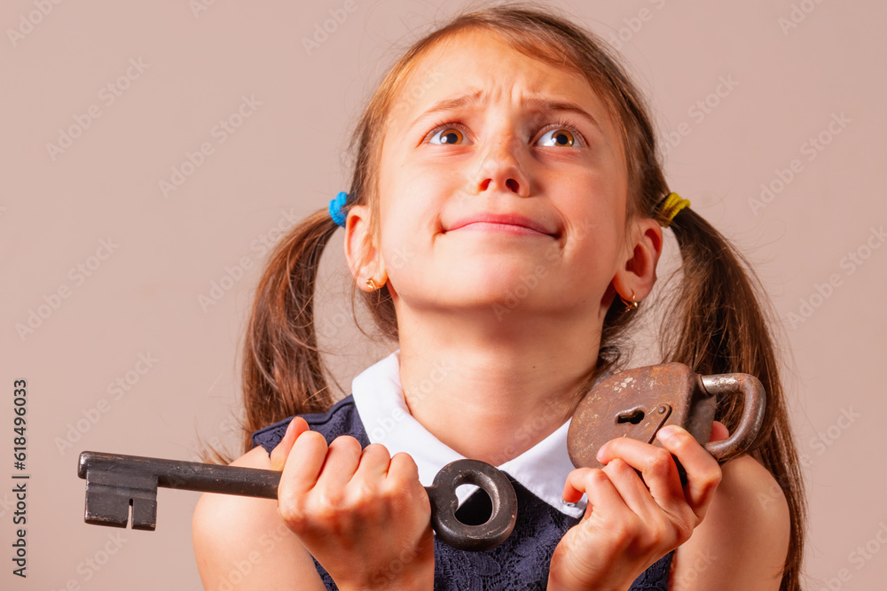 Confused beautiful young girl holding big key and small lock as symbo ...