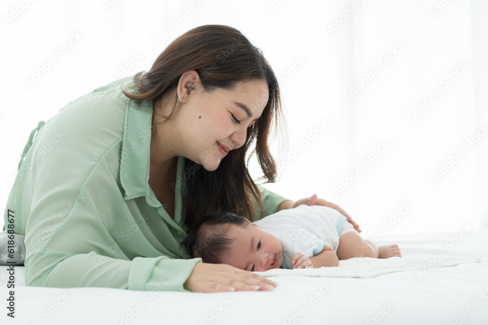 Happy Asian young mother takes care and kissing her newborn baby on white bed. Asian newborn ...