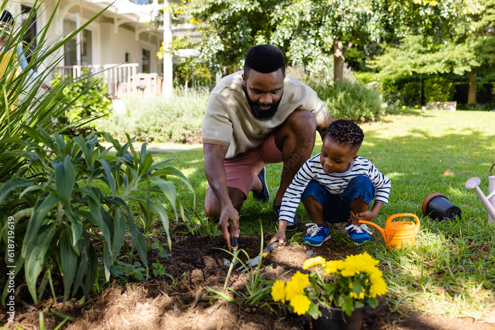 African american father and son digging dirt with tools on grassy field ...