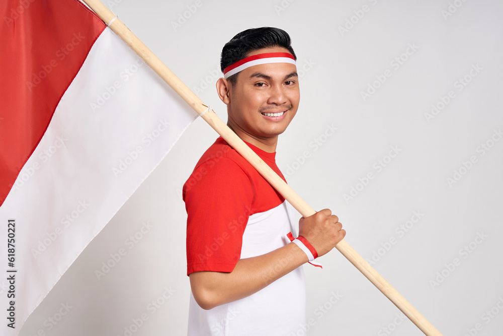 Smiling happy young Asian man holding an Indonesian flag isolated over ...