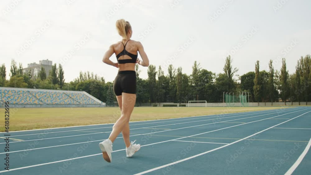 Back view of sporty tall blonde running on athletics track in the ...