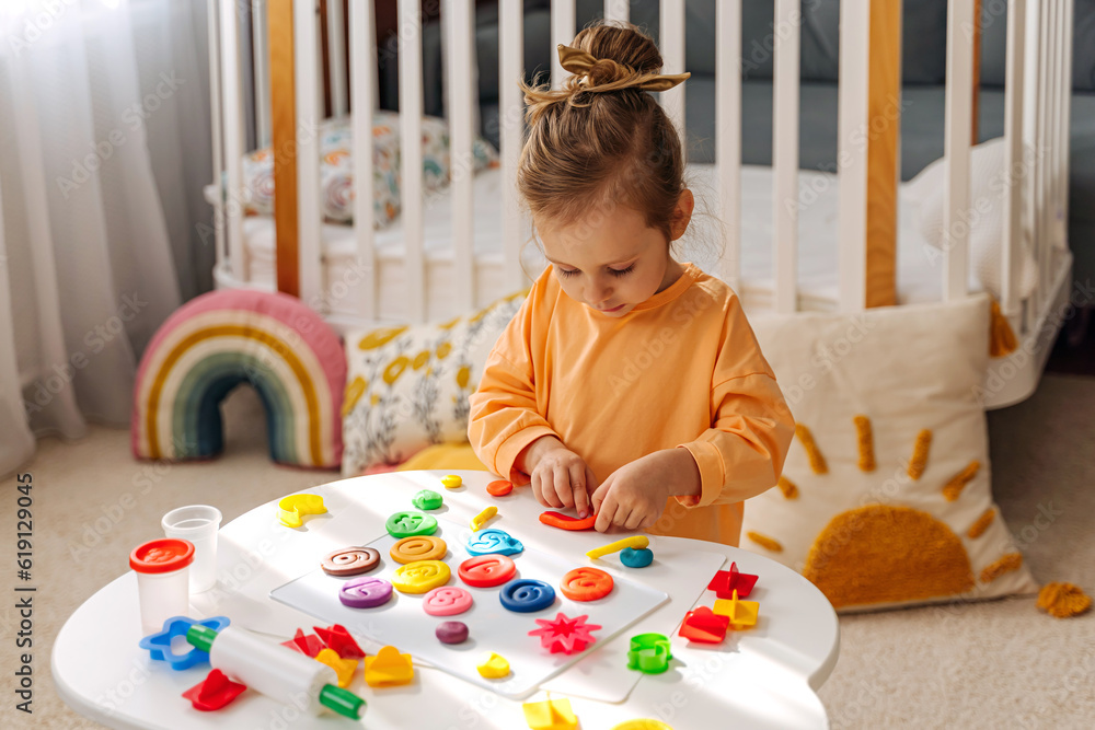 A little girl play with plasticine and creates colorful numbers ...