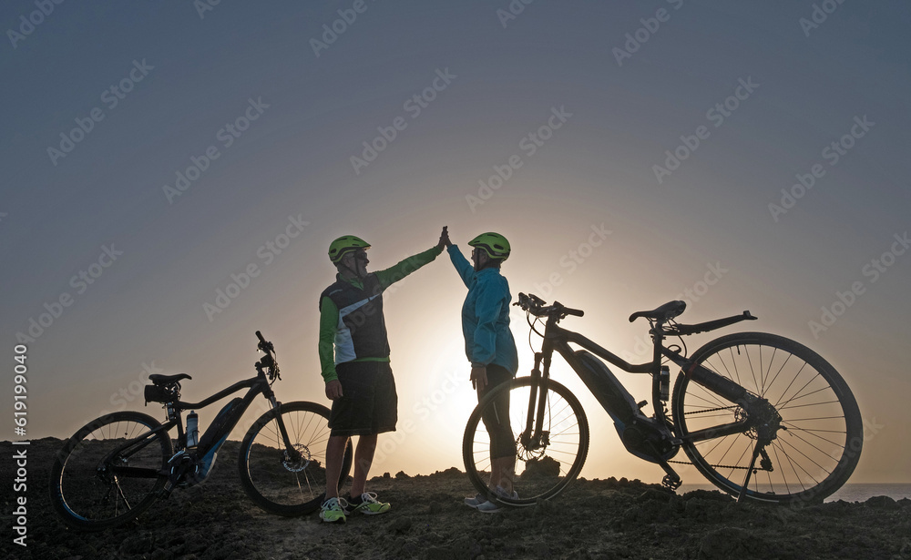 Silhouette of senior couple of cyclists running bicycles in footpath at ...