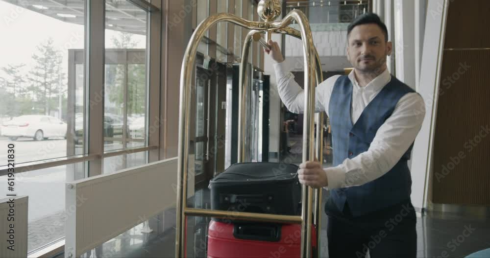 Dolly shot of helpful bellman pushing trolley with luggage along hotel ...