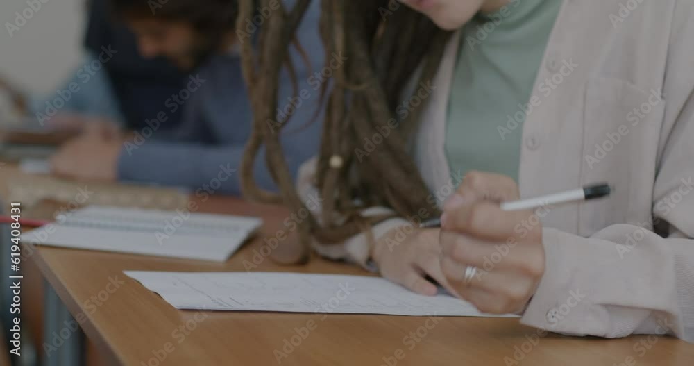 Close-up of hand with pen passing examination while woman student ...