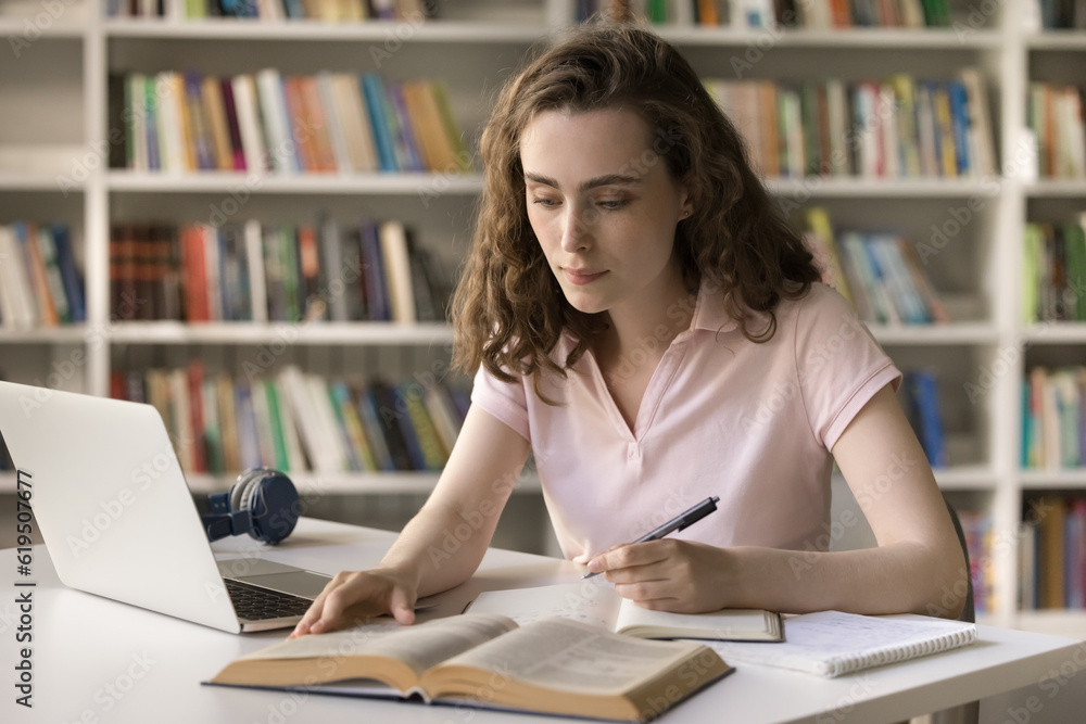 Serious focused pretty student girl studying in campus library, reading ...