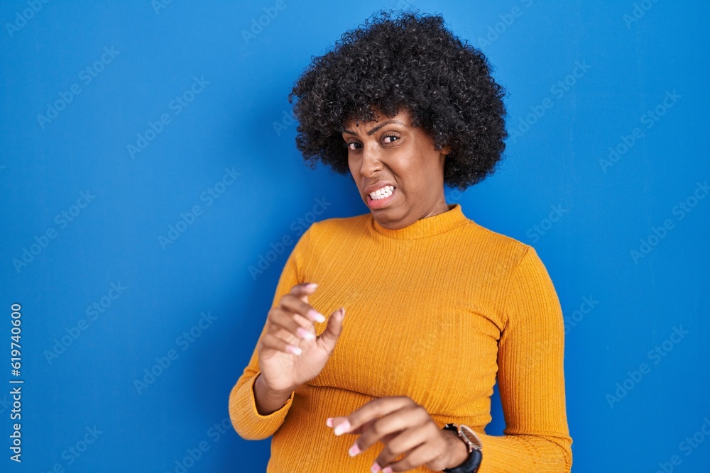 Black woman with curly hair standing over blue background disgusted ...