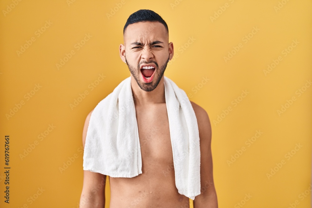 Young hispanic man standing shirtless with towel angry and mad ...