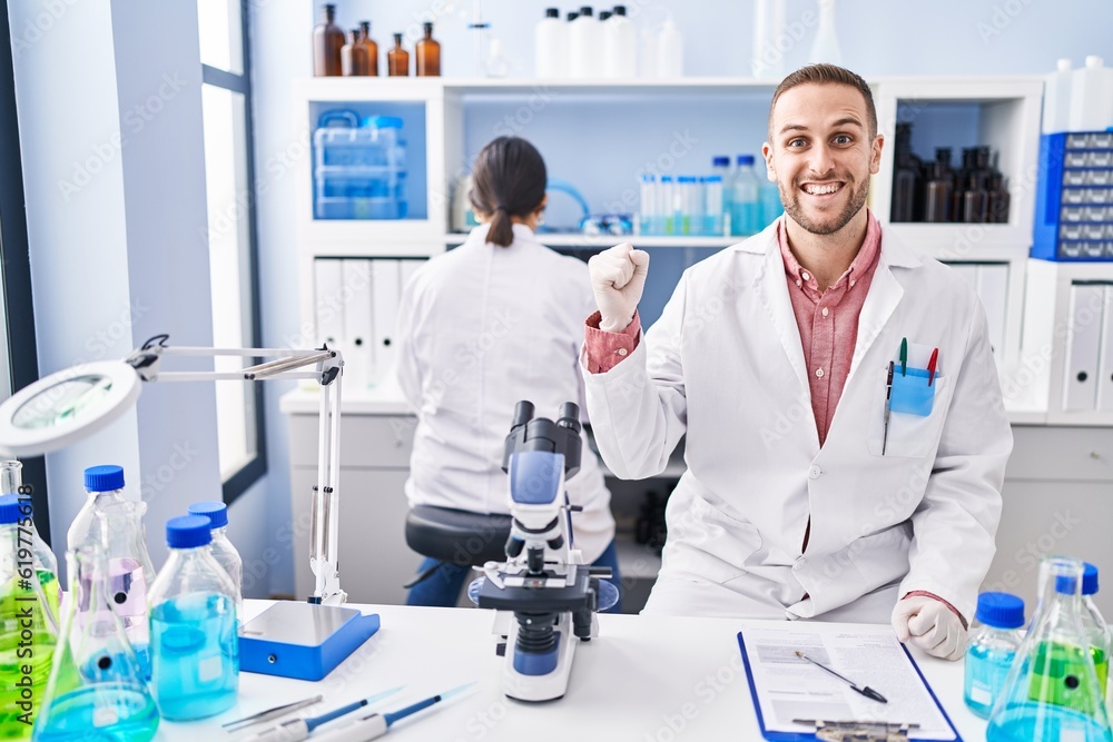 Young man working at scientist laboratory screaming proud, celebrating ...