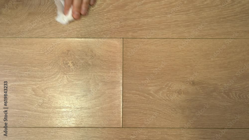 Hand wipes water from swollen laminate floor with napkin and dries with ...