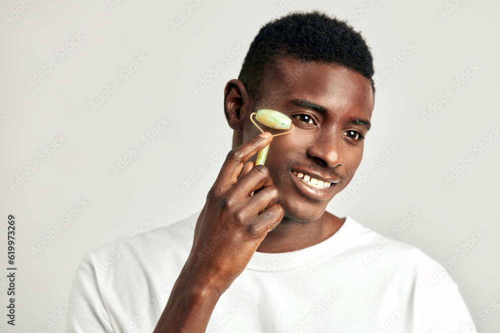 Black guy with youthful skin using jade de-puffing face roller to keep ...