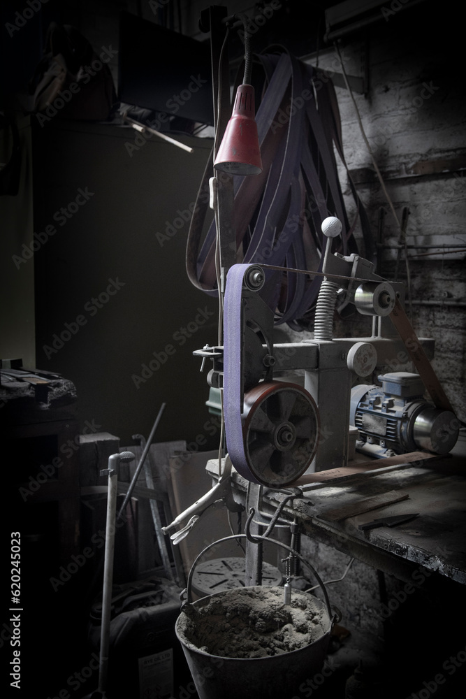 Man in a dark forge grinding a knife with a belt grinder and sparks ...