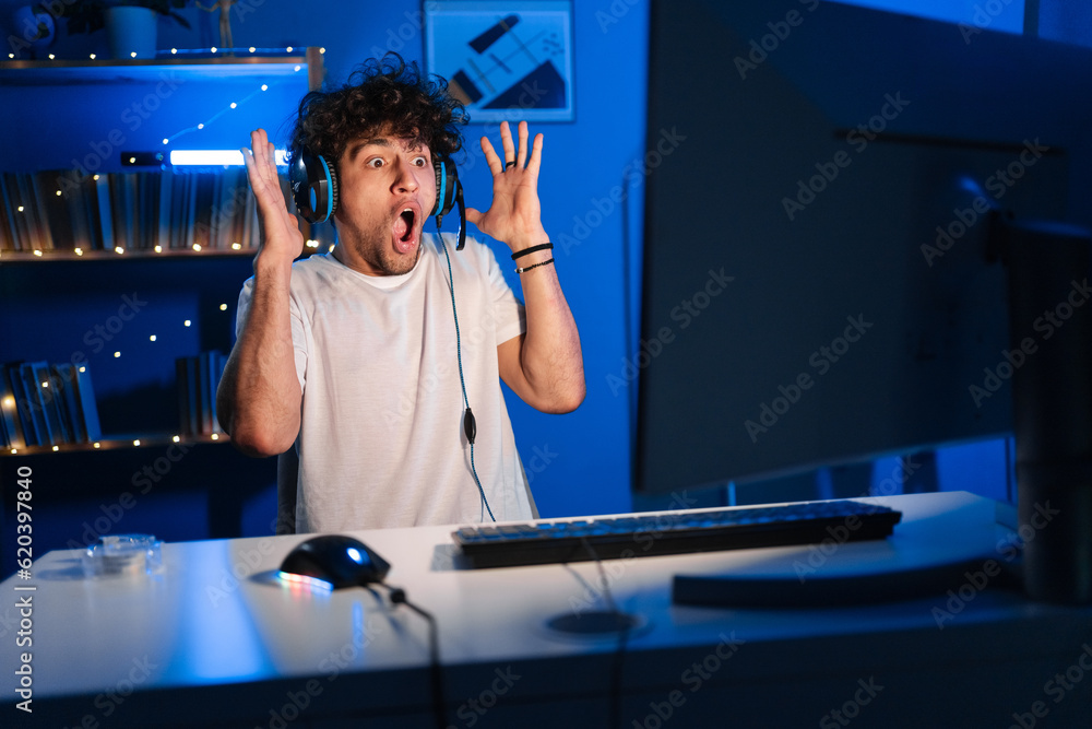 Shocked young arabic gamer wearing headphones screaming playing video ...