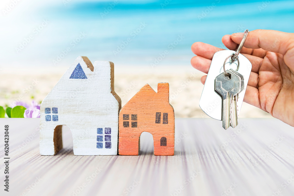 House key in girl hand with wooden house model over blurred beach ...