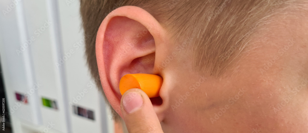 Boy inserting ear plugs into ears to get rid of noise in loud place ...