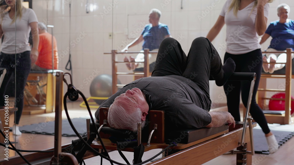 Pilates coach assisting senior man to use machine to strengthen body ...
