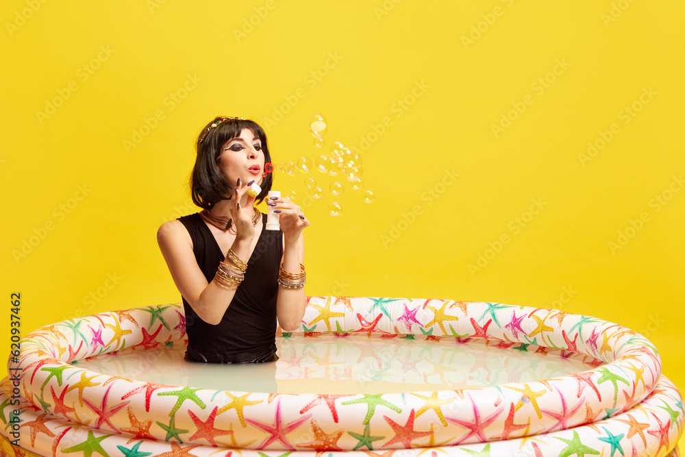 Pretty young woman in image of Cleopatra sitting in swimming pool with ...