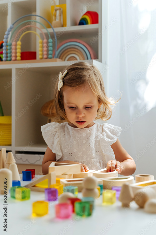 A little girl playing with wooden blocks on the table in playroom ...