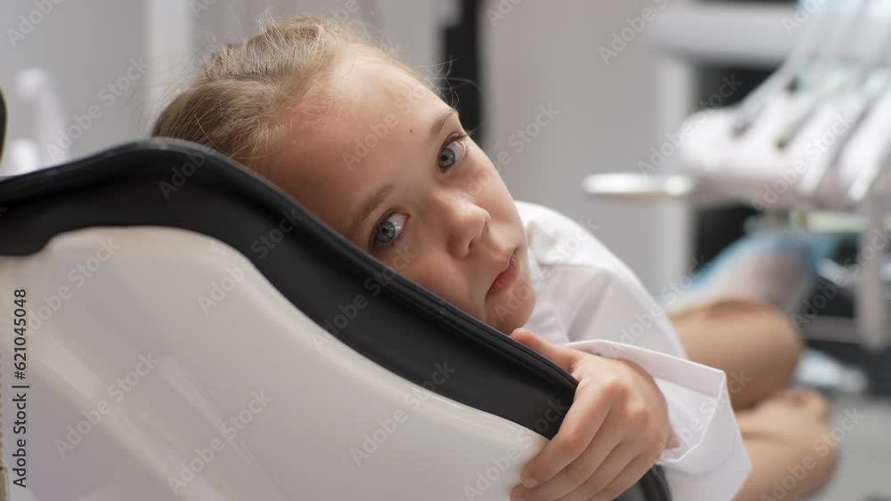 Close-up portrait of afraid little girl lying in dental chair sadness ...