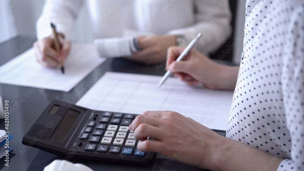 Two accountants use a calculator and laptop computer for counting taxes ...