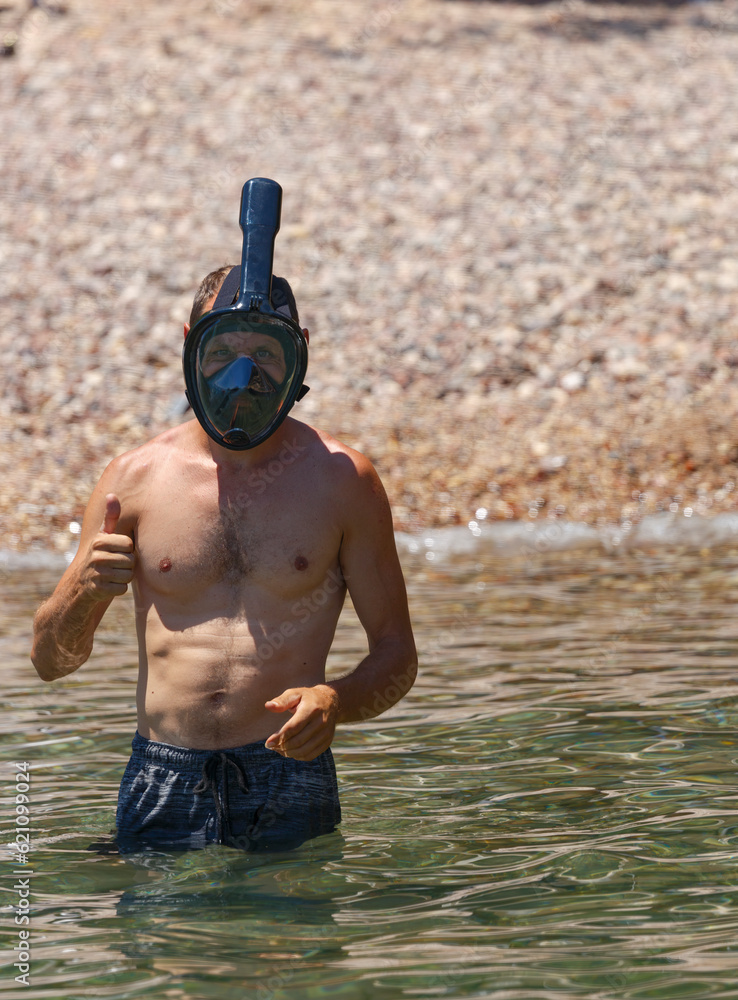Young man wearing diving face scuba on beach. Shirtless man make thumbs ...