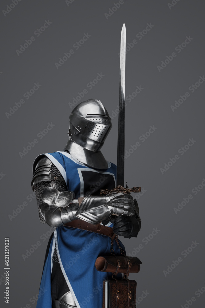 Medieval guard dressed in armor and blue surcoat holding a sword ...