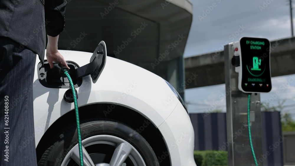 Businesswoman recharge her electric car from charging station at city ...