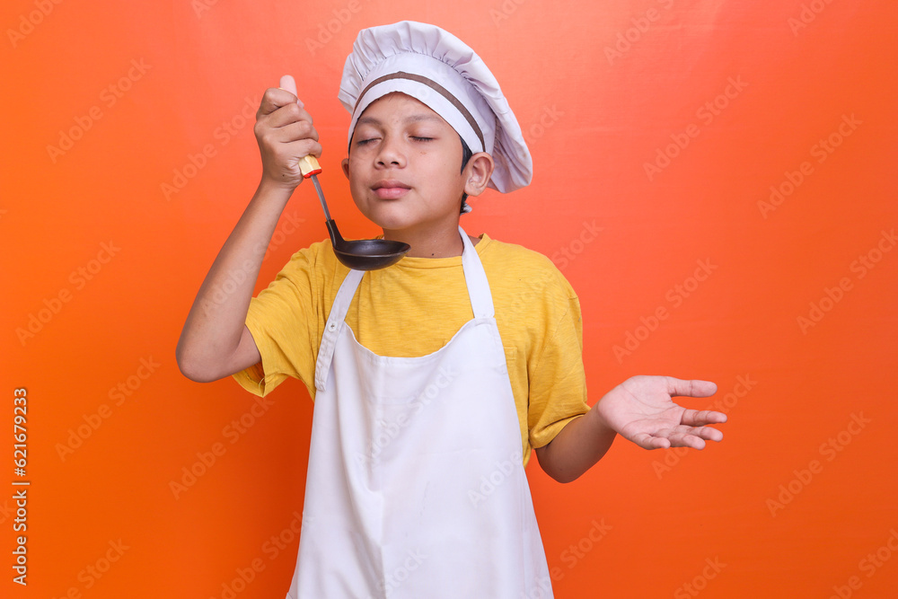 Portrait of little boy cook holding a soup ladle and smelling it with ...