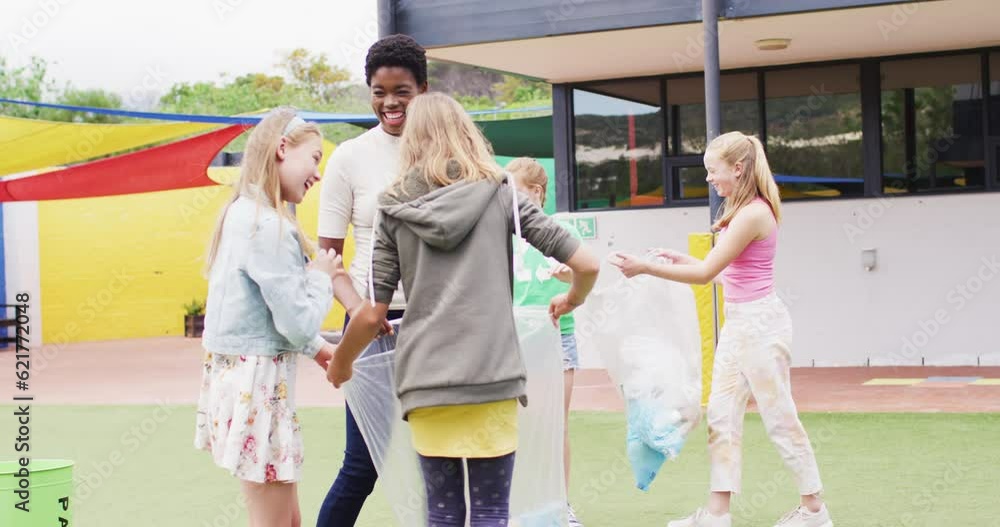 Diverse female teacher and happy schoolchildren cleaning together with ...