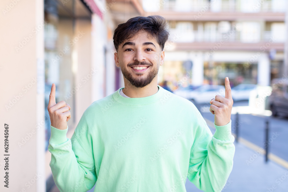 young handsome man feeling awed and open mouthed pointing upwards with ...