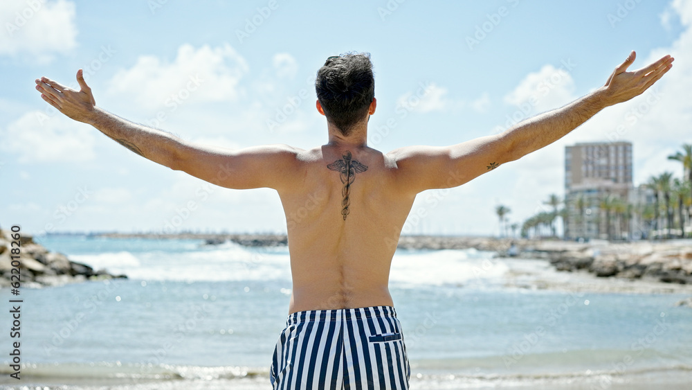 Young hispanic man tourist wearing swimsuit standing backwards with ...