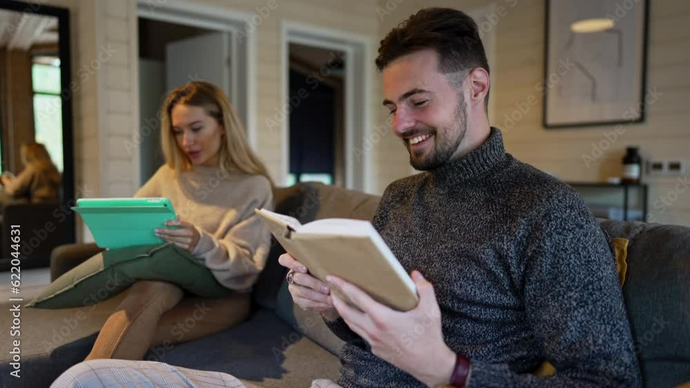Laughing positive man reading book out loud as woman scrolling digital ...
