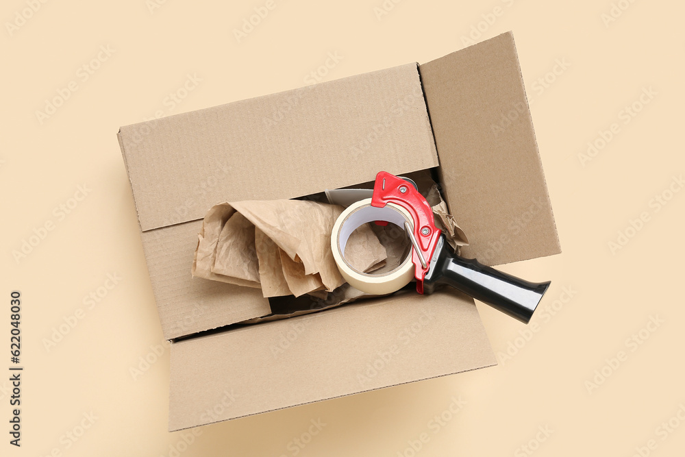 Packing tape dispenser and cardboard box on beige background Stock ...